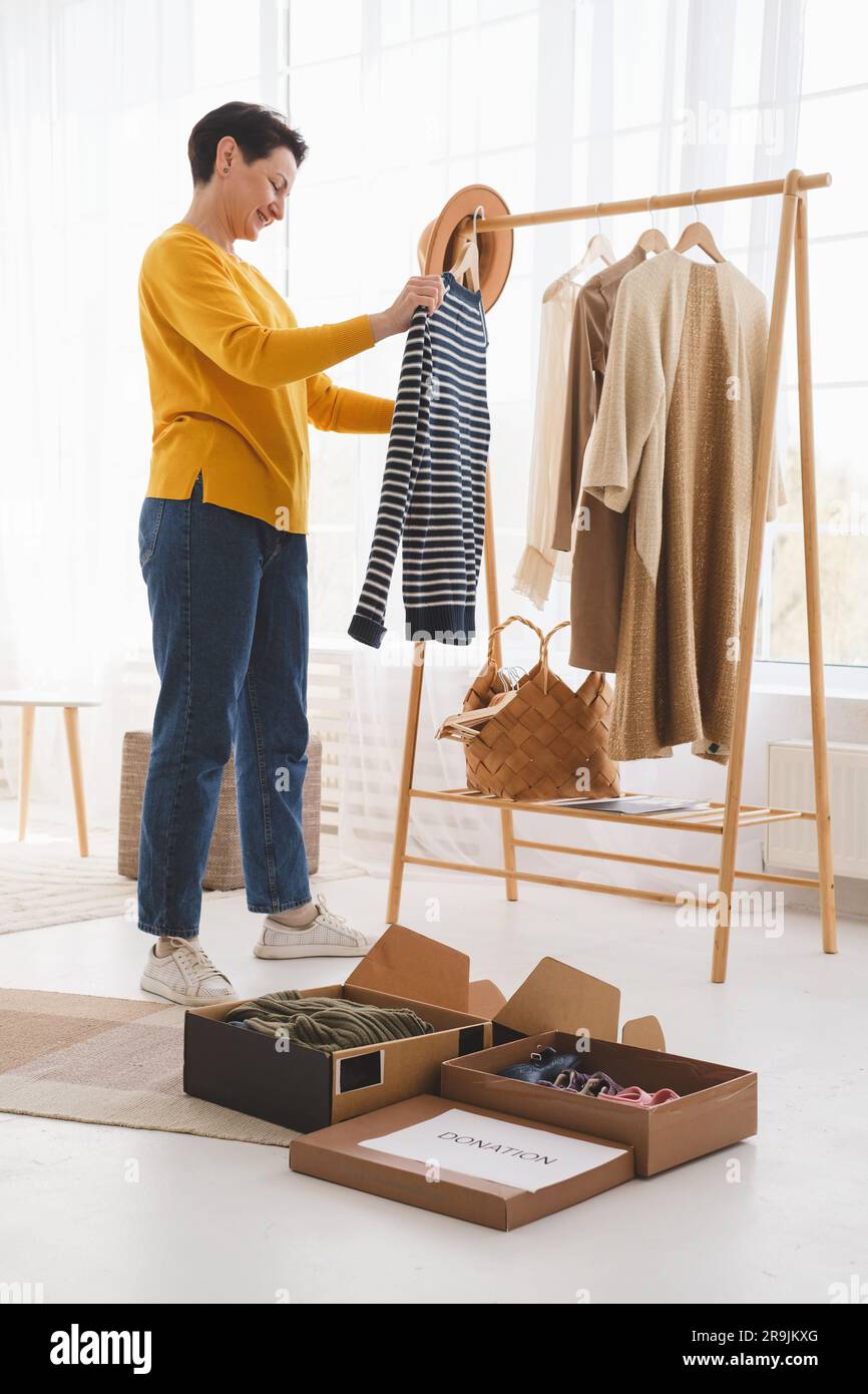 Happy middle aged woman in casual outfit standing near wooden hanger ...