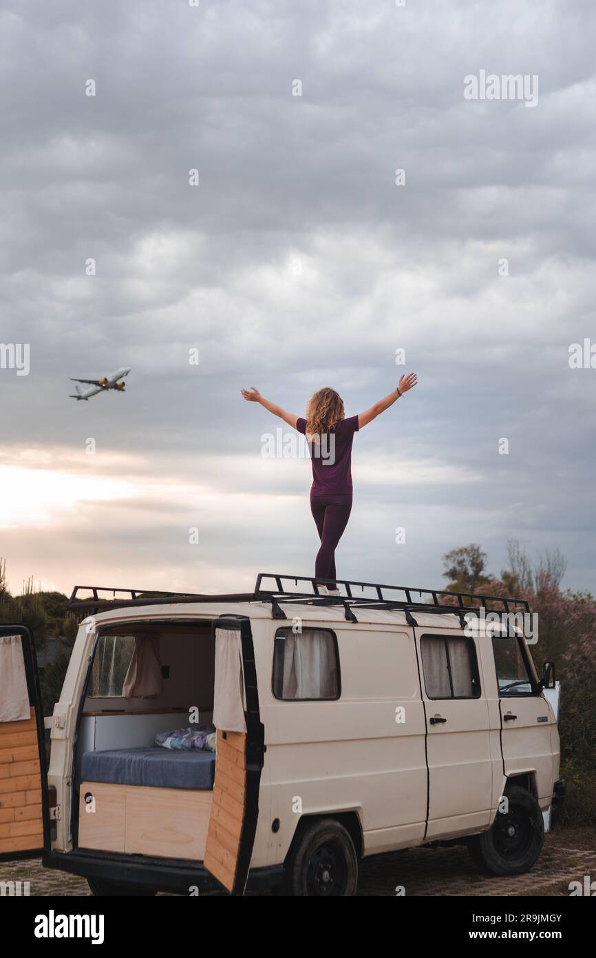 Back view of young traveler in trainers standing on parked van top with ...