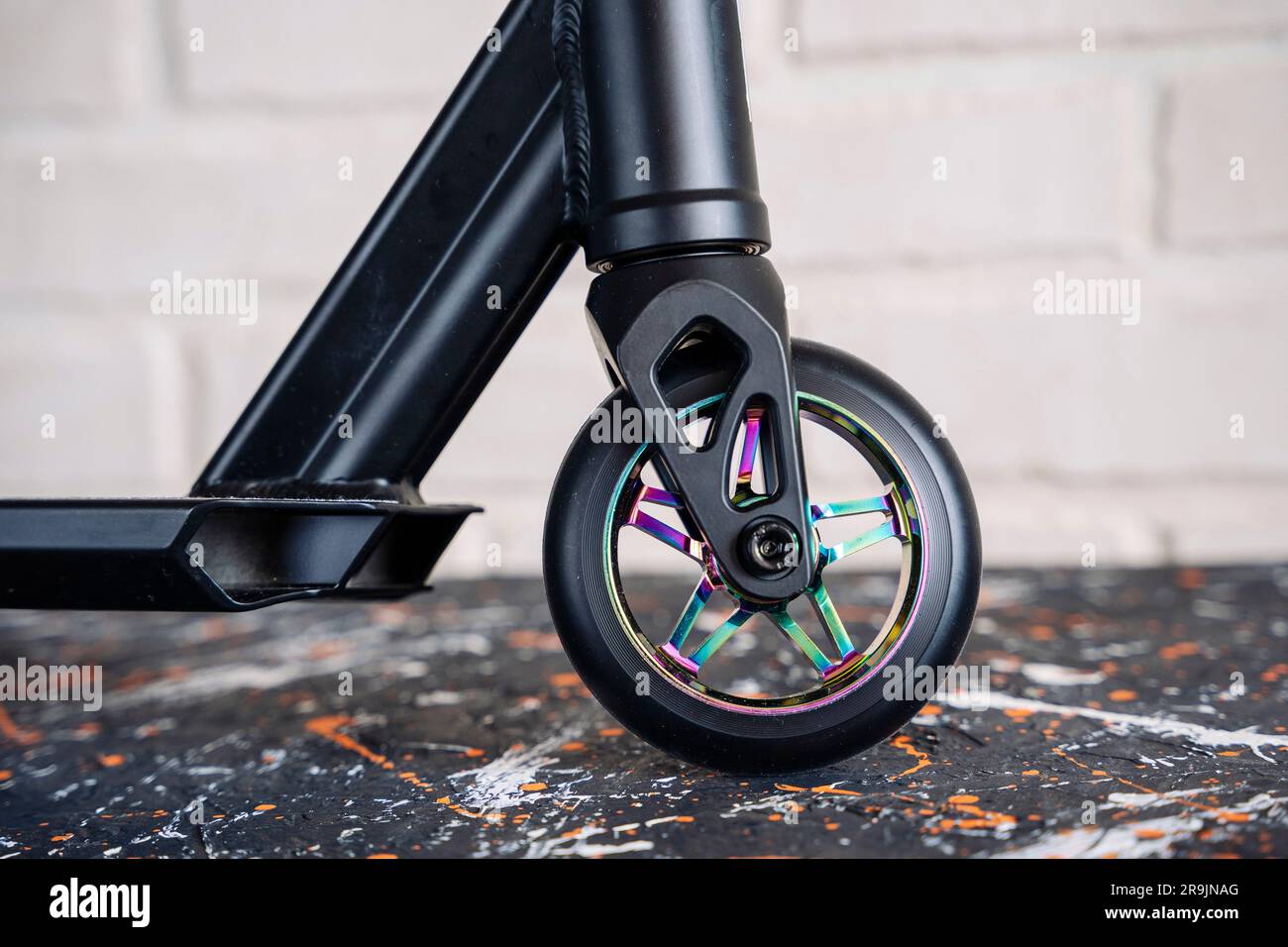 The front wheel of a rainbow-colored stunt scooter against a light ...