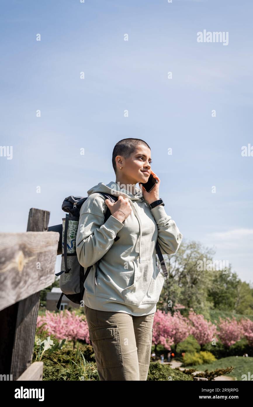 Smiling young short haired female tourist with backpack and map talking on smartphone and ...