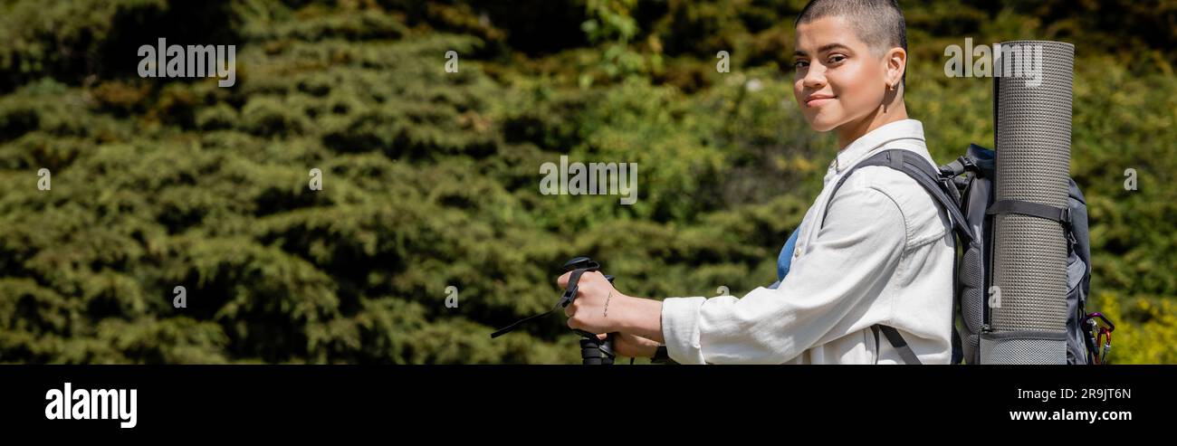 Positive young short haired woman hiker with backpack looking at camera ...