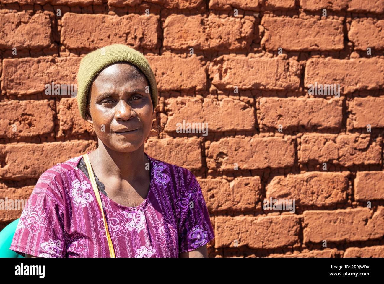 Portrait of a Malawian women sitting against a brick wall in a rural ...