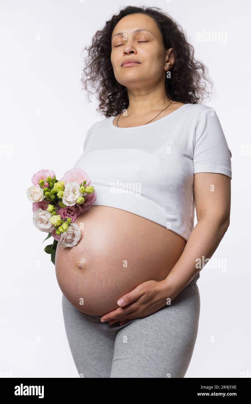Delightful pregnant woman with bouquet of flowers, caressing her big ...