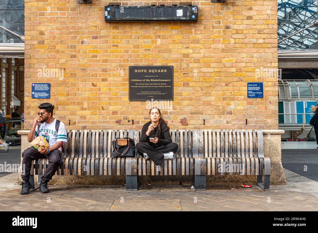 A man and woman sit in a bench beneath a plaque for Hope Square outside ...