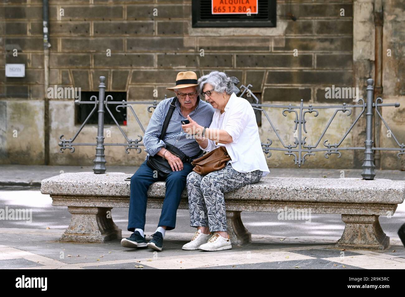 Older couple on a stone bench looking at their mobile phones, Palma de ...