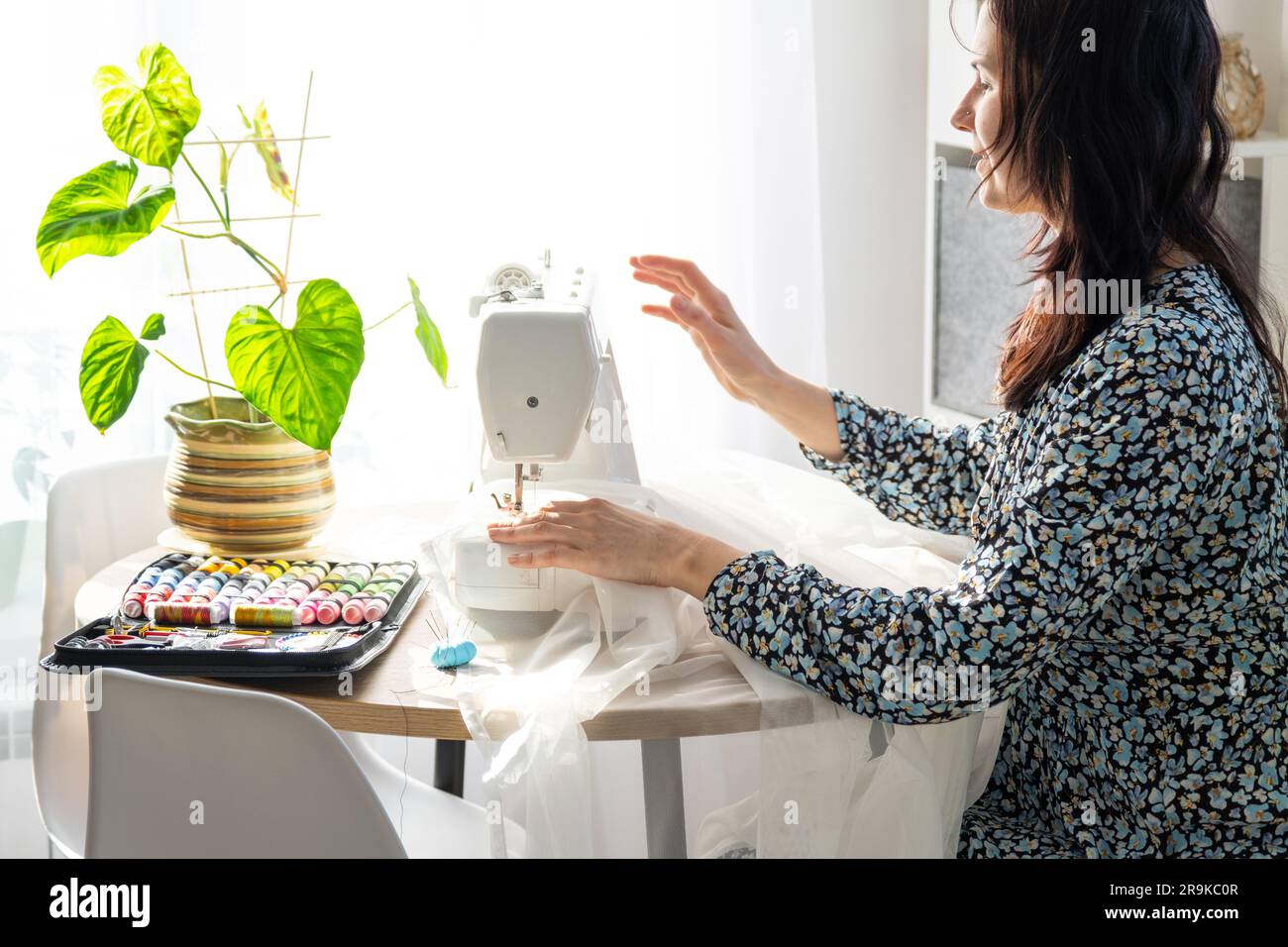 A woman sews tulle on an electric sewing machine in a white modern ...