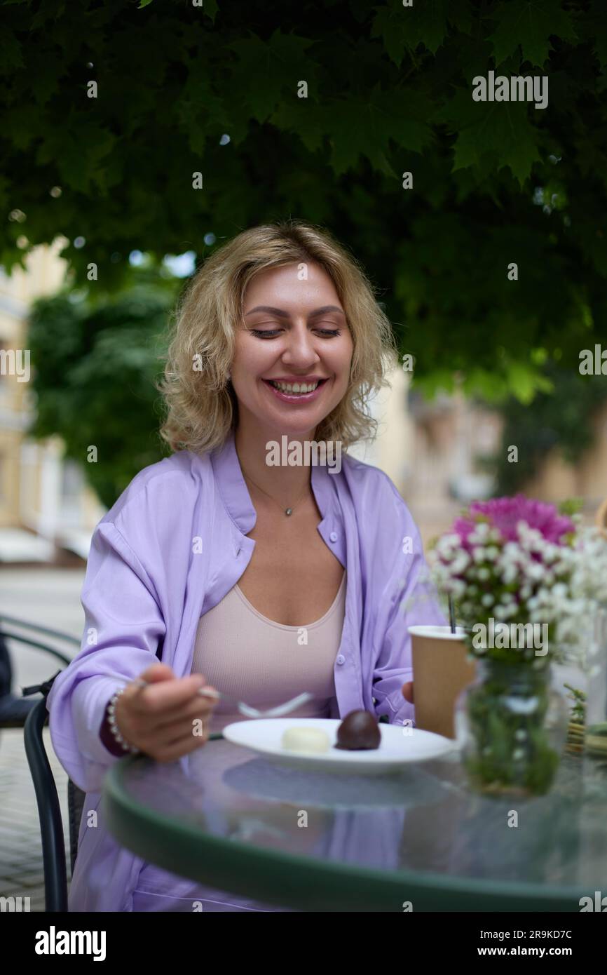 Happy young woman eating a chocolate candy in a outdoor cafe. Portrait ...