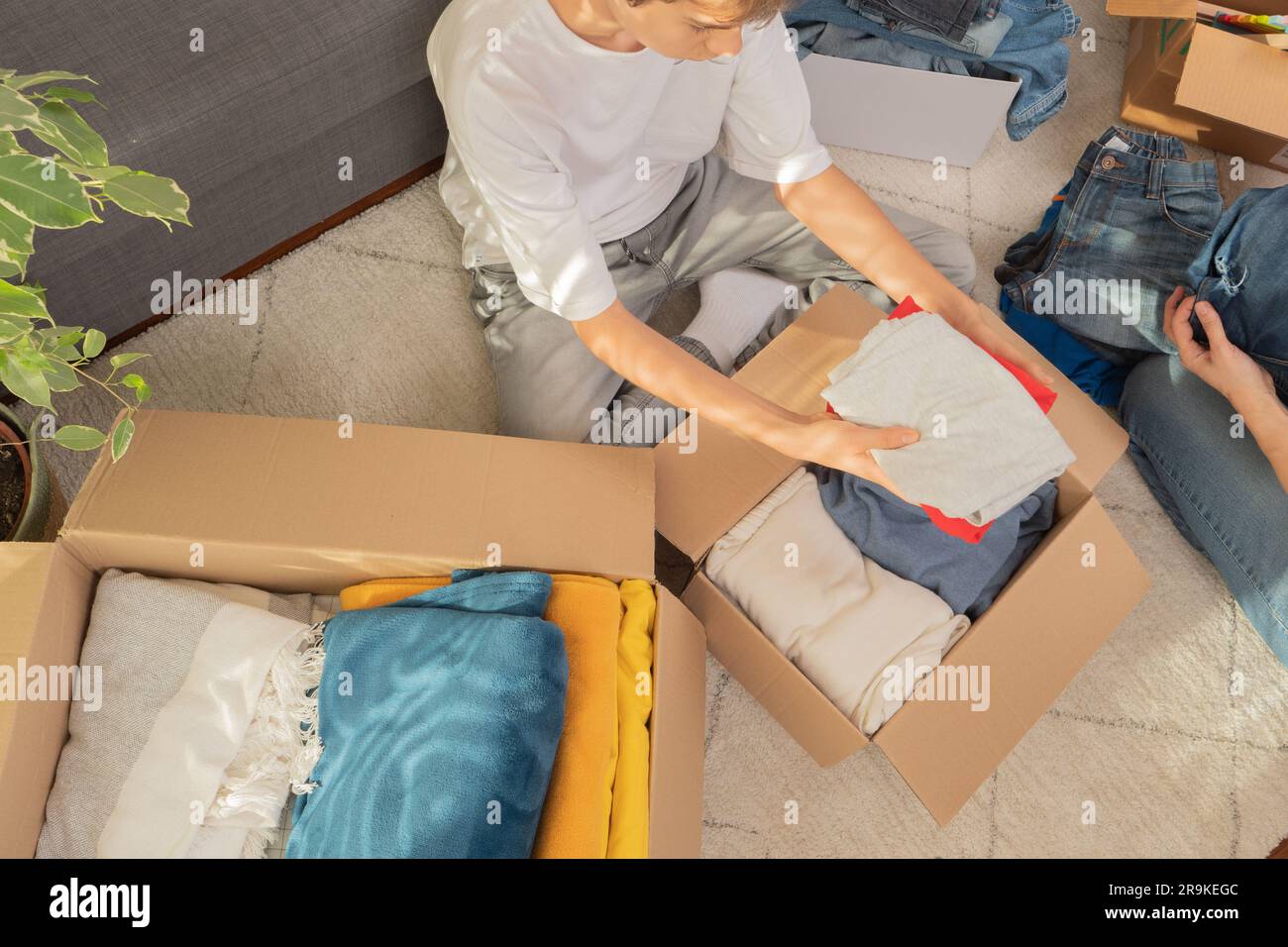 Mother and son sorting clothes and packing into cardboard box. Donations for charity, help low ...