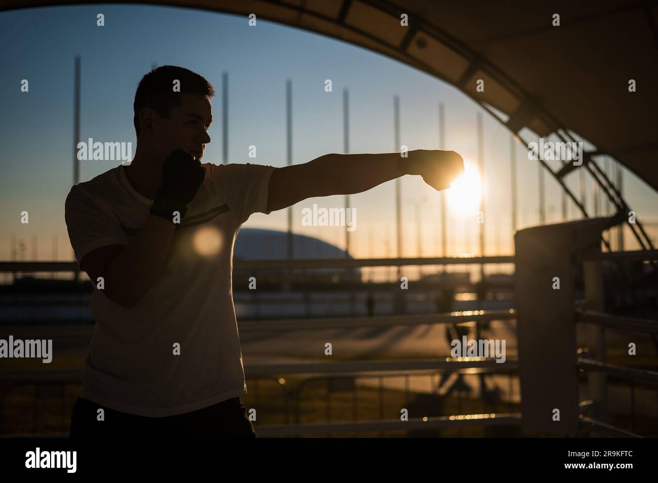 A man trains in boxing at the stadium at sunset. Athlete silhouette ...