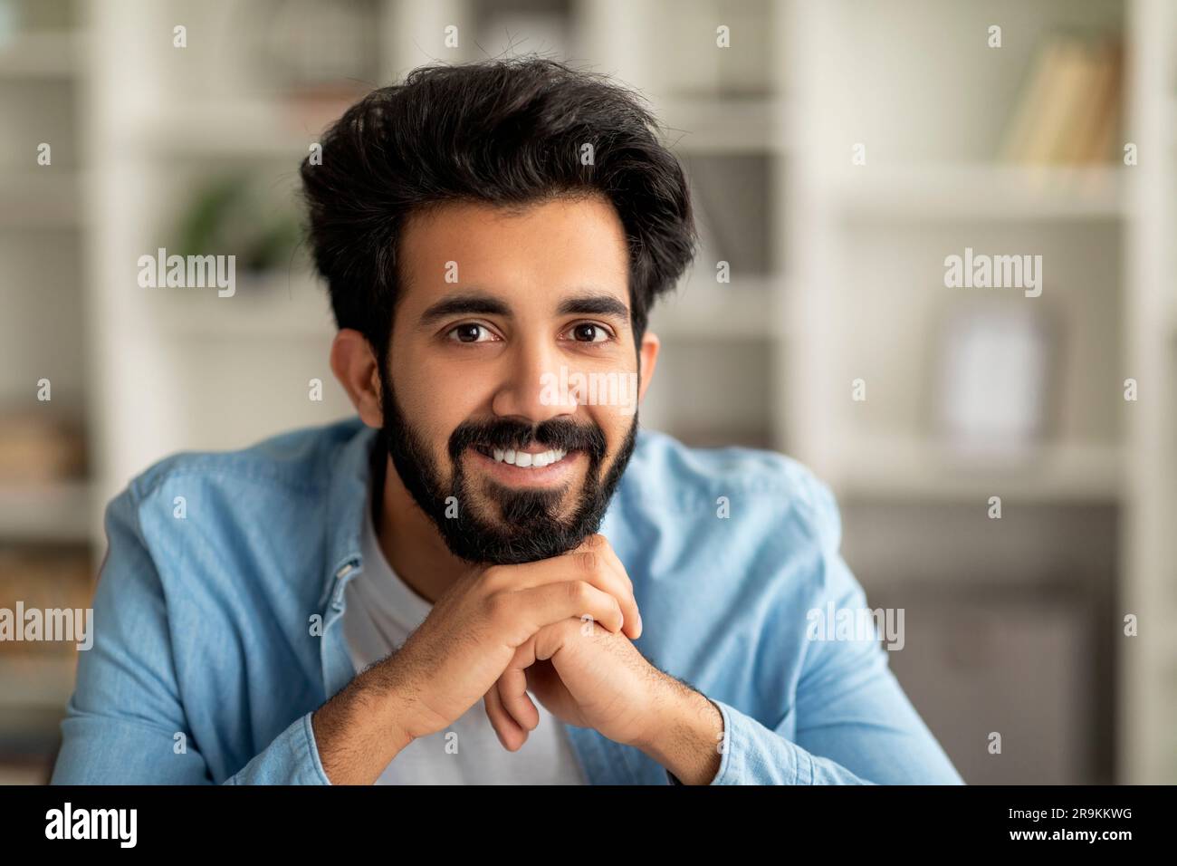Handsome cheerful indian man resting chin on hands and looking at ...