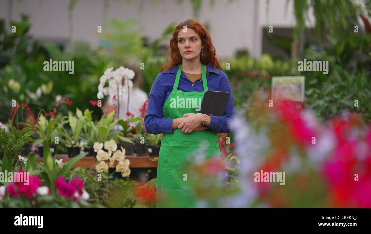 Candid pensive female Florist employee standing inside flower shop ...