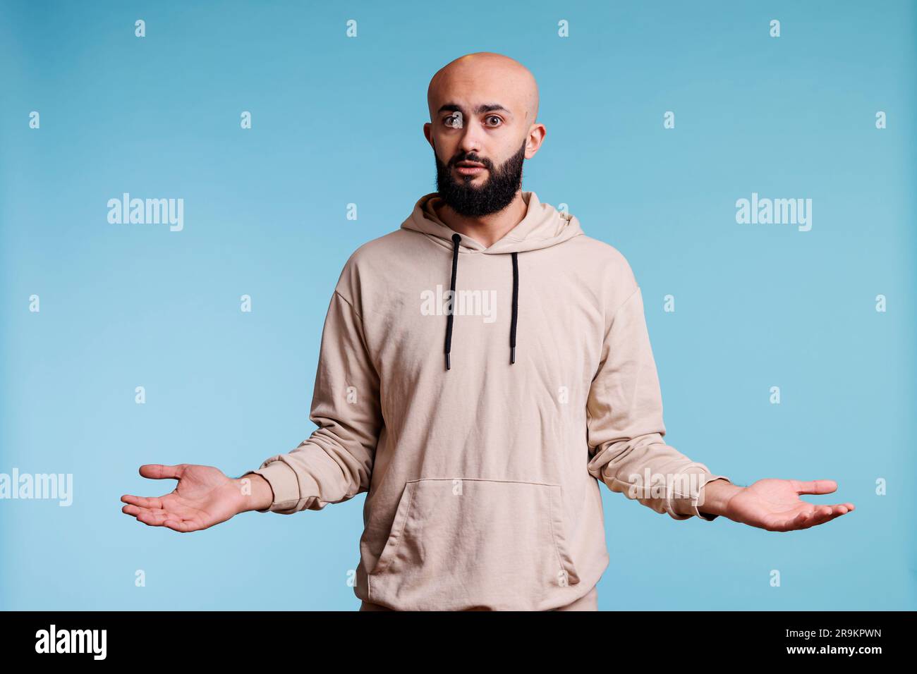 Arab man standing in confusion, shrugging shoulders and looking at ...