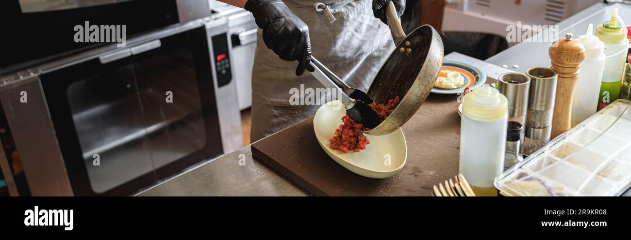 Chef putting ready dish from frying pan into the plate before serving ...