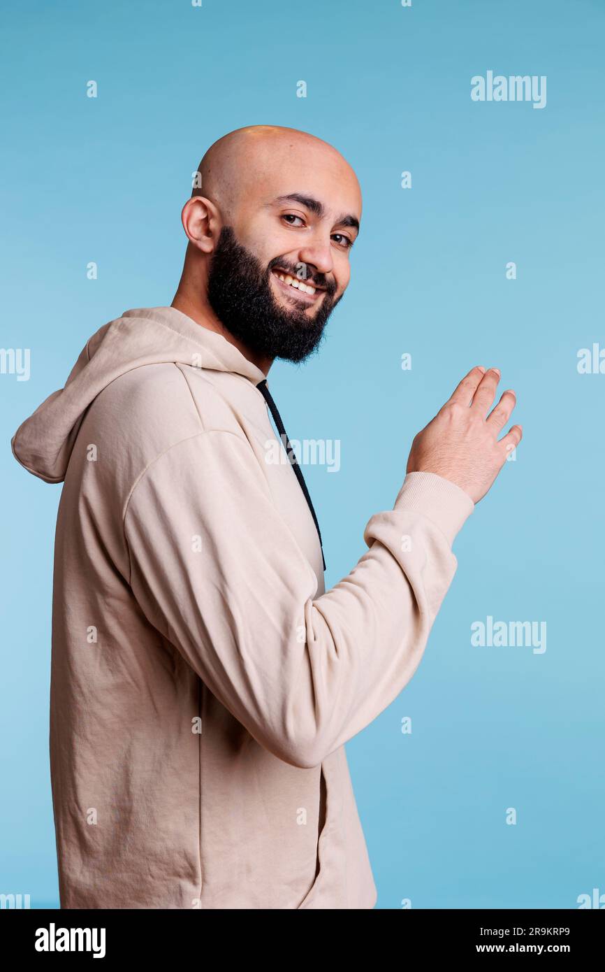 Smiling arab man inviting with arm gesture and looking at camera with ...