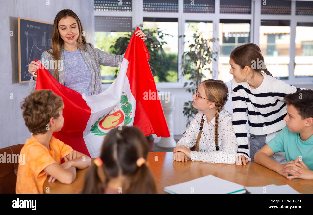 Excited young female teacher showing flag of Peru to schoolchildren ...