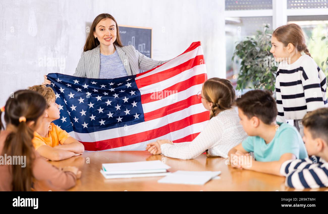 Smiling young woman teacher showing national flag of USA and telling ...