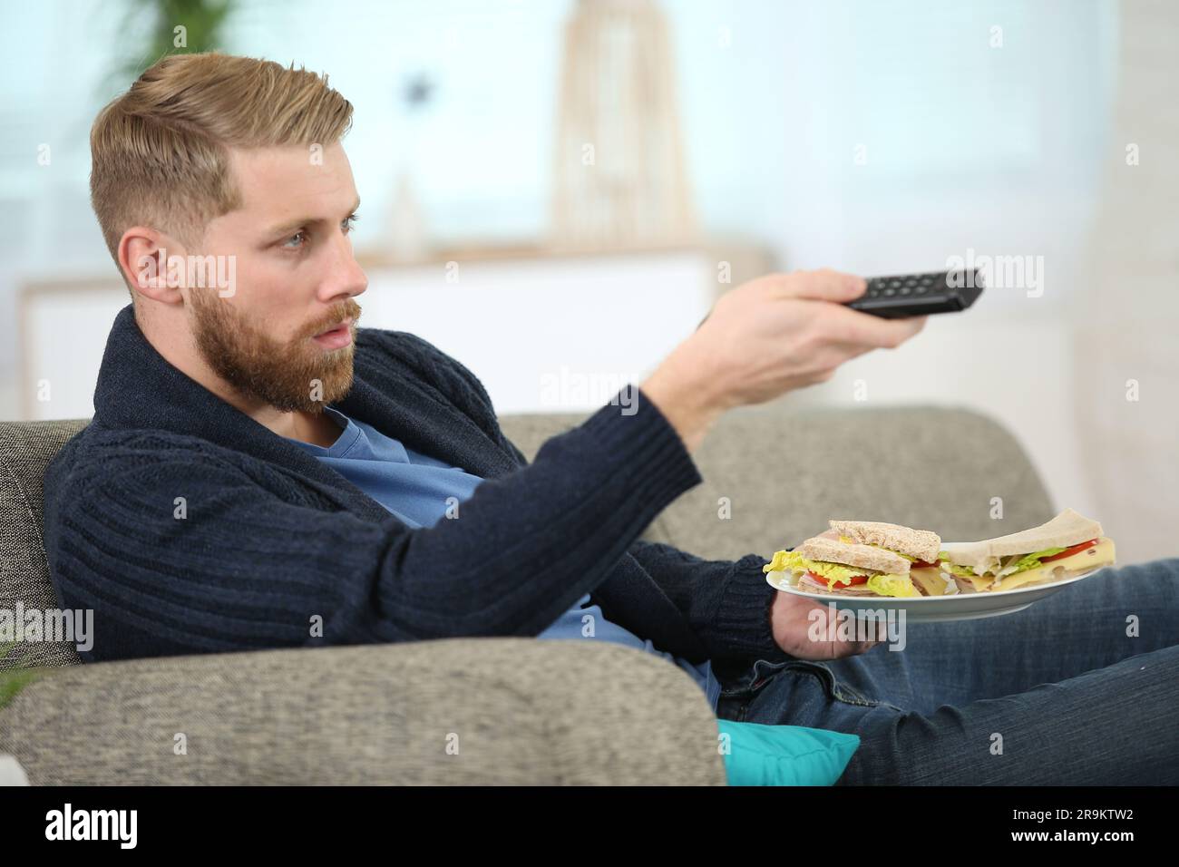 man changing tv channel with remote control while eating sandwich Stock ...