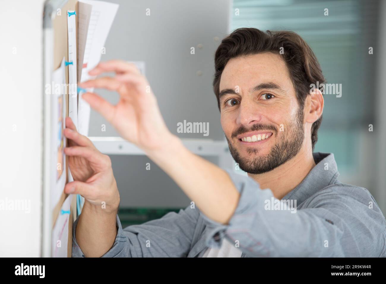 smiling man pins poster on notice board Stock Photo - Alamy