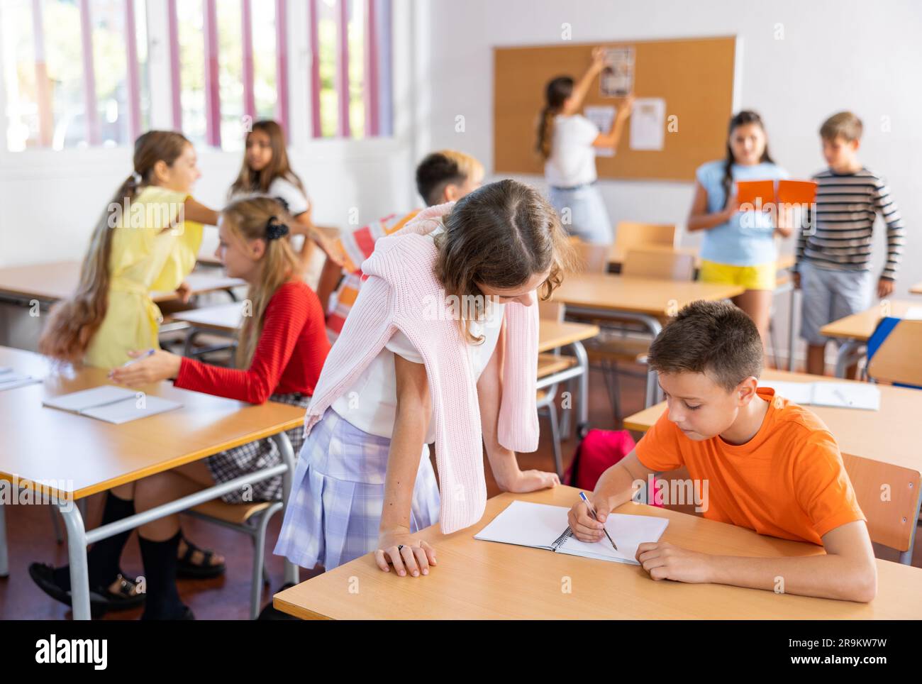 Tween girl helping classmate to complete written assignment in class ...