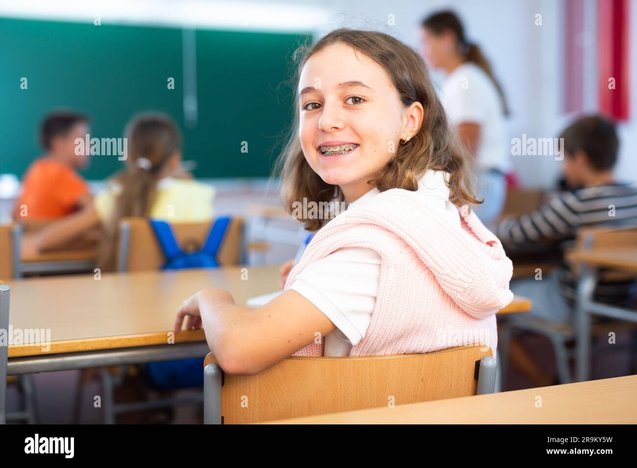 Schoolgirl sits half-turned at desk in classroom at lesson in ...