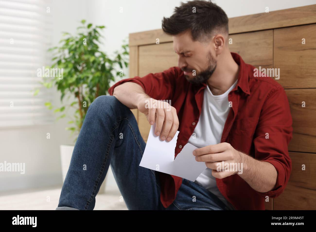 Sad man ripping photo on floor indoors. Divorce concept Stock Photo - Alamy
