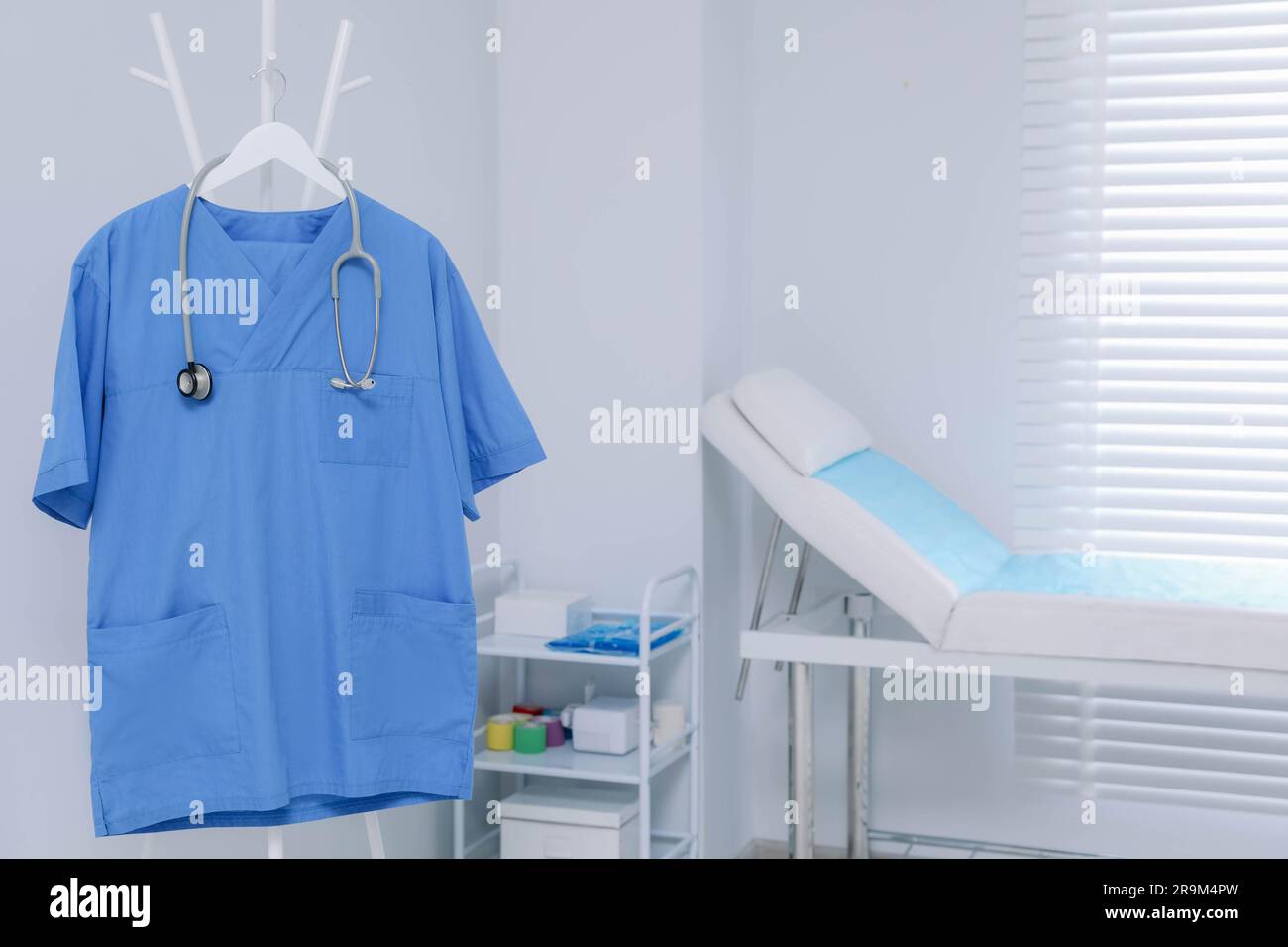 Blue medical uniform and stethoscope hanging on rack in clinic. Space ...