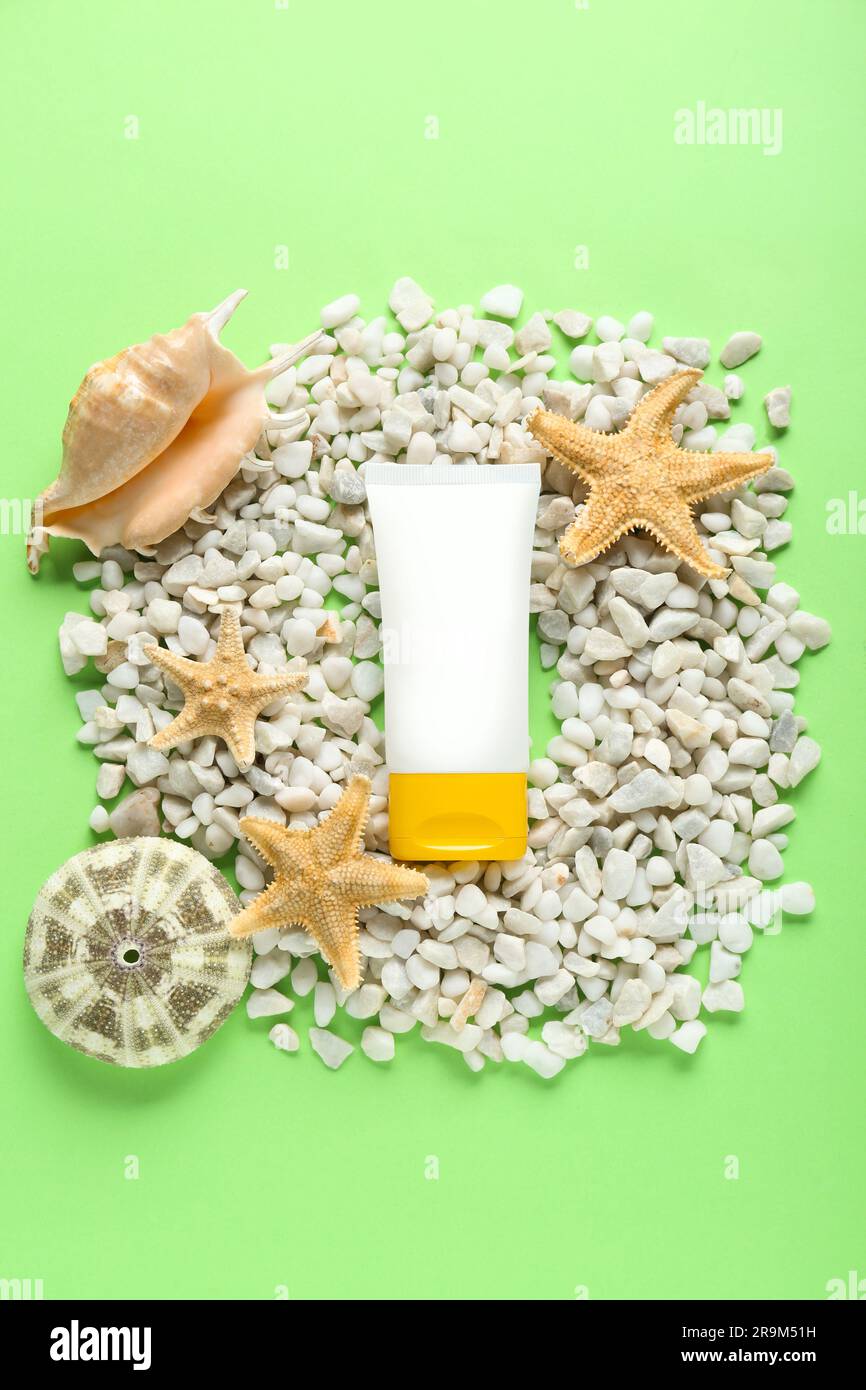 Suntan cream tube, seashells and white marble pebbles on light green ...