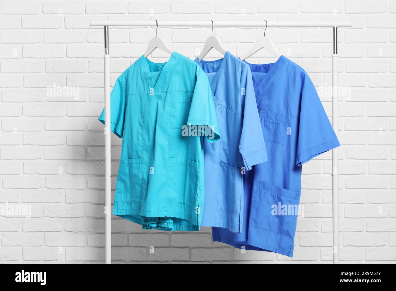 Medical uniforms hanging on rack near white brick wall Stock Photo - Alamy