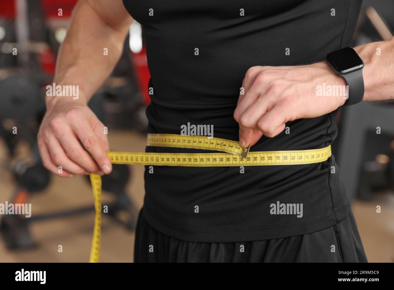 Athletic man measuring waist with tape in gym, closeup Stock Photo - Alamy