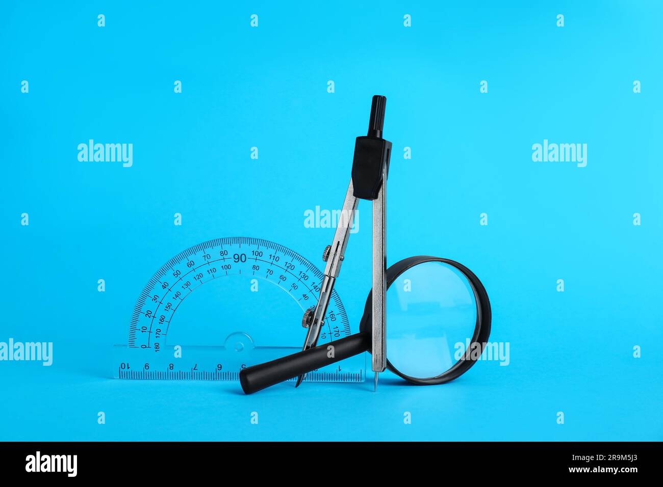 Protractor, magnifying glass and compass on light blue background Stock ...