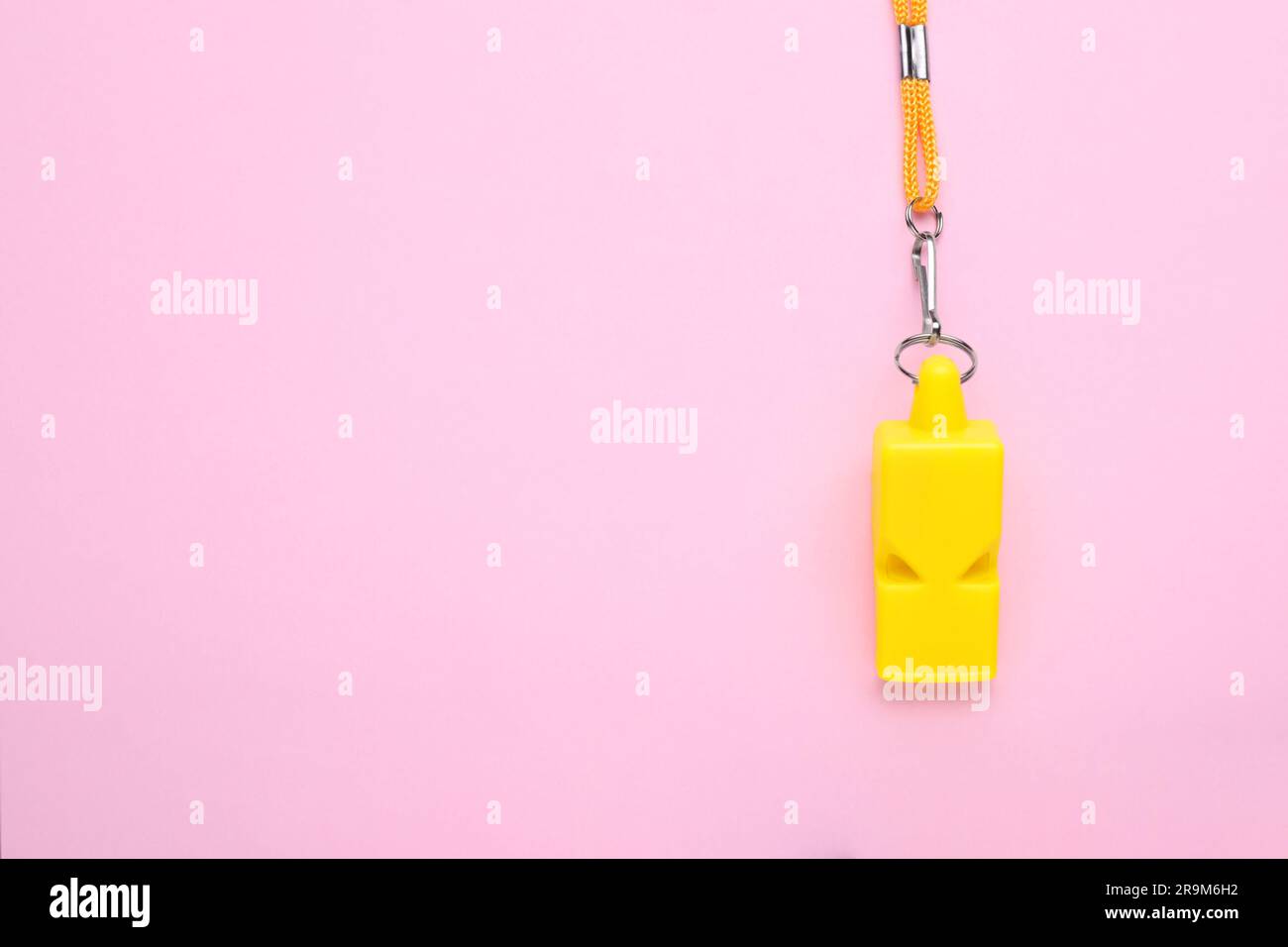 One yellow whistle with orange cord on pink background, top view. Space ...