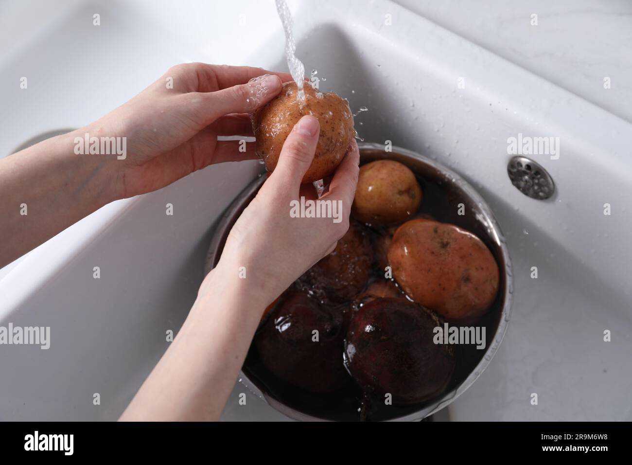 Woman washing fresh potato in kitchen sink, closeup. Cooking ...