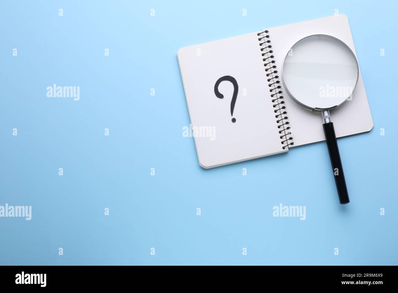 Magnifying glass and notebook with question mark on light blue ...