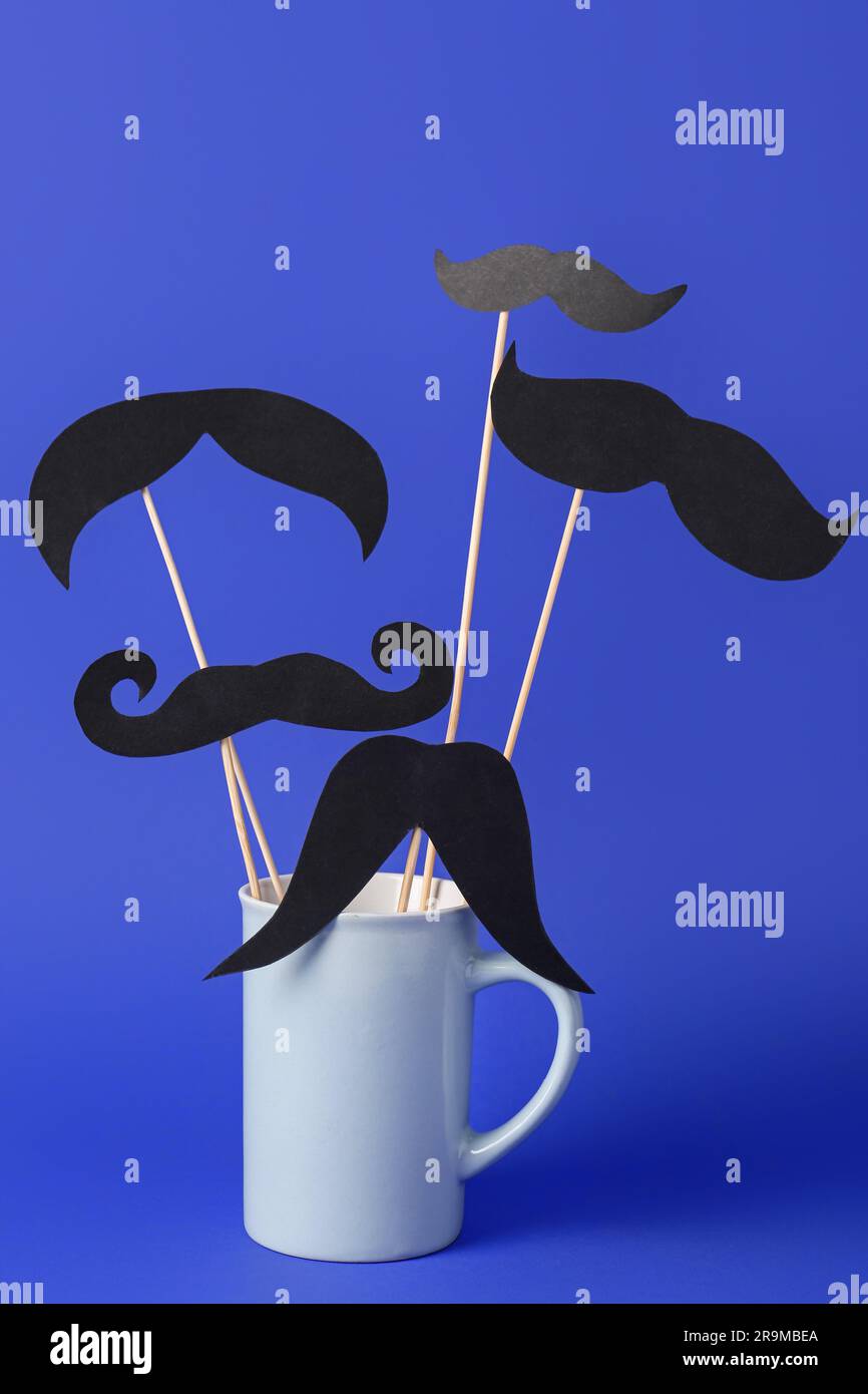 Wooden sticks with different paper mustaches in cup against blue ...