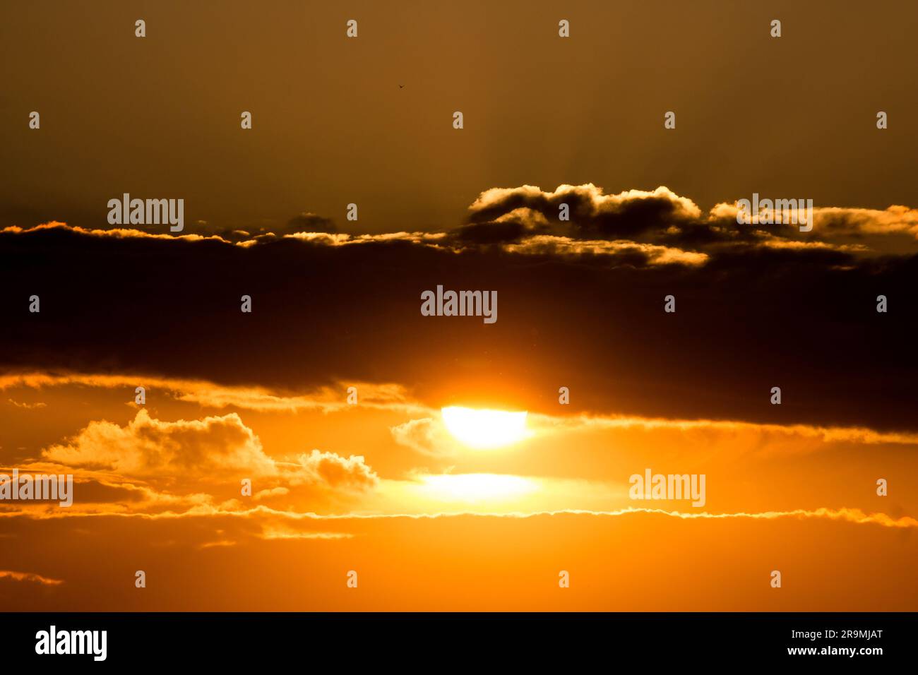 Bright orange sun peeking out from behind dark clouds Stock Photo - Alamy