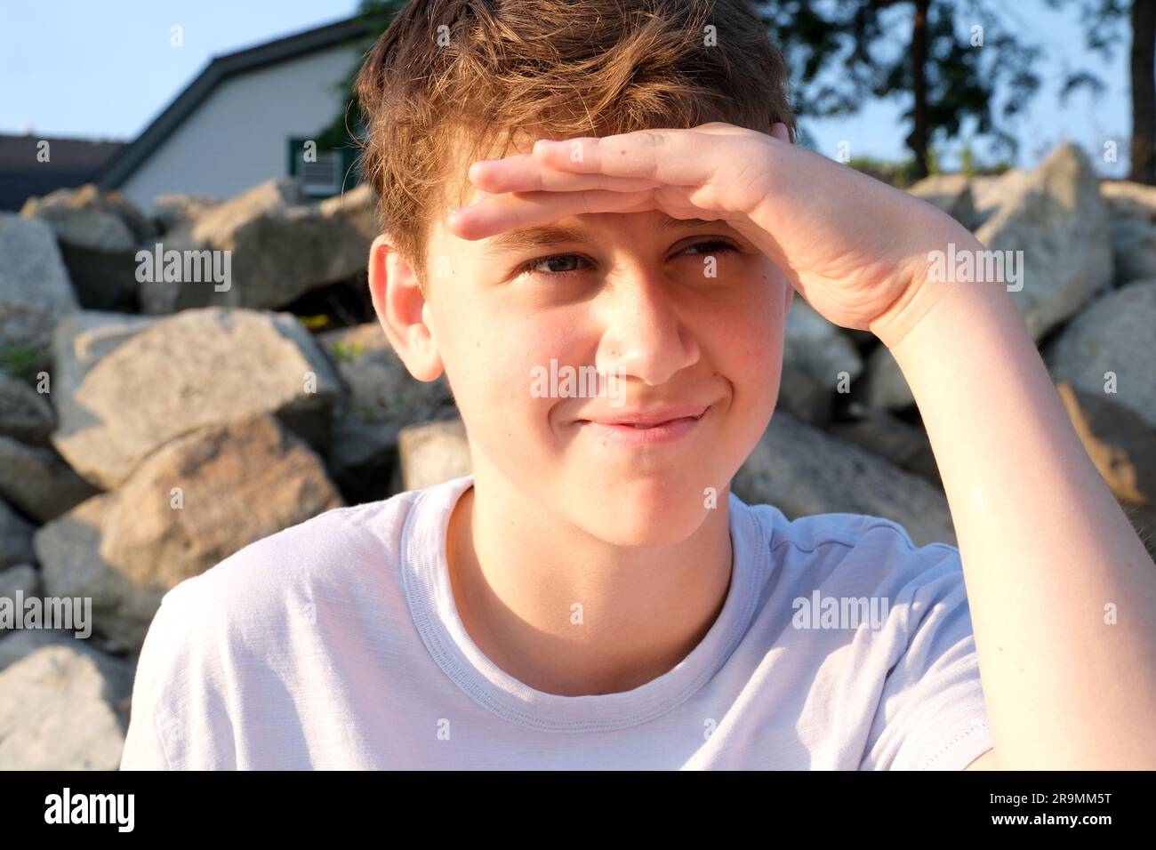 boy teenager 14-16 years old looks into distance smiling covers the sun ...