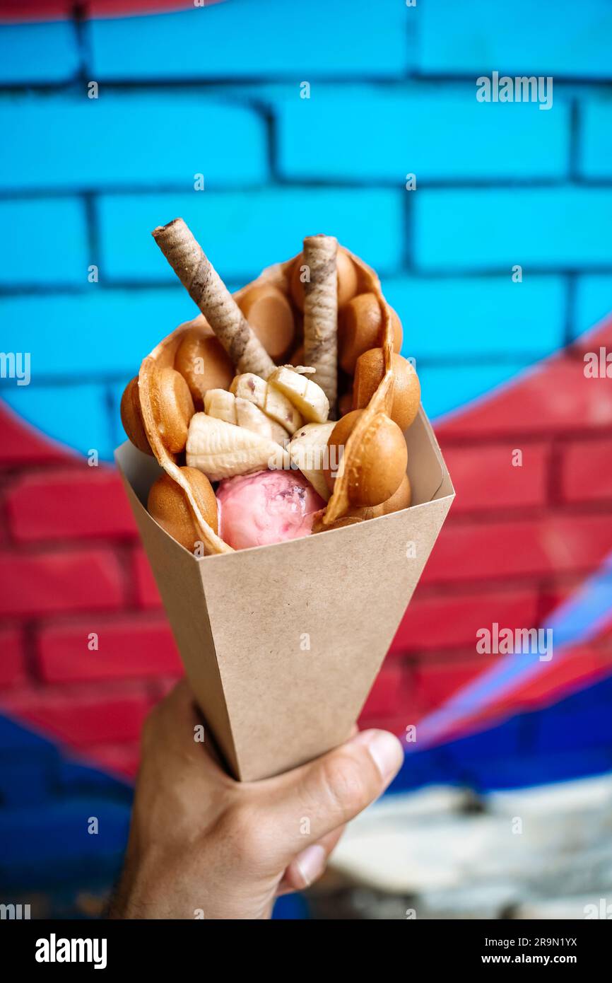 Street food dessert Belgian waffles in hand on a colored wall ...