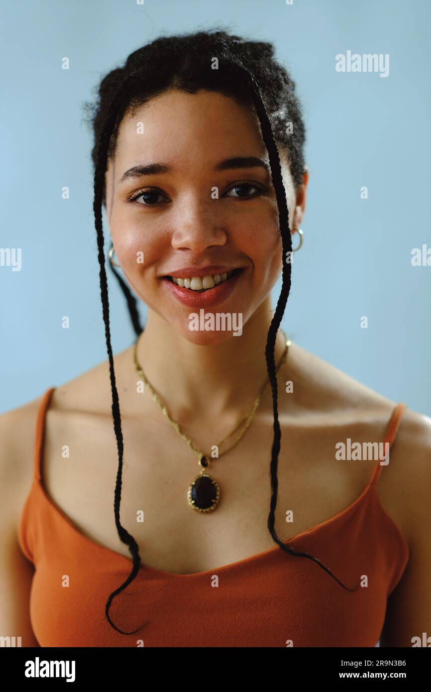 Smiling young adult woman with braids. She wears orange tank top in ...