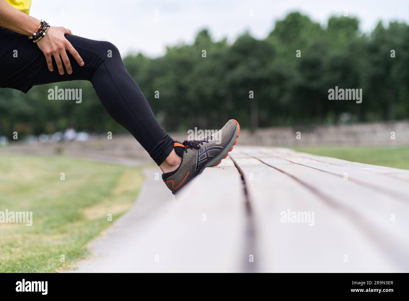 Man wearing black leggings touching sports shoe toe cap leaning on ...