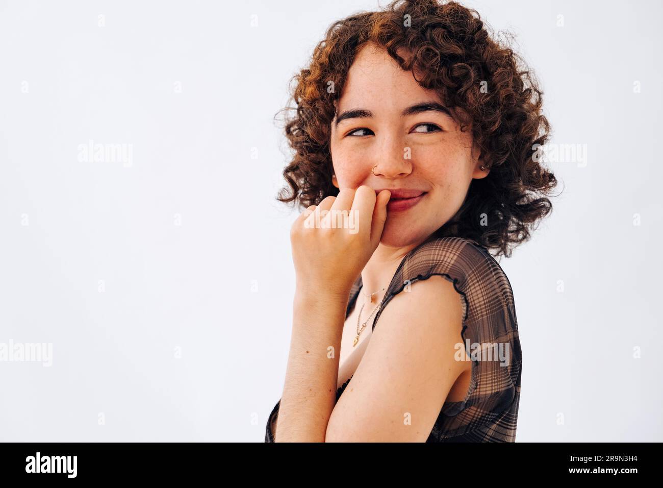 woman mischievous smiling looking away with hand on chin curly hair ...