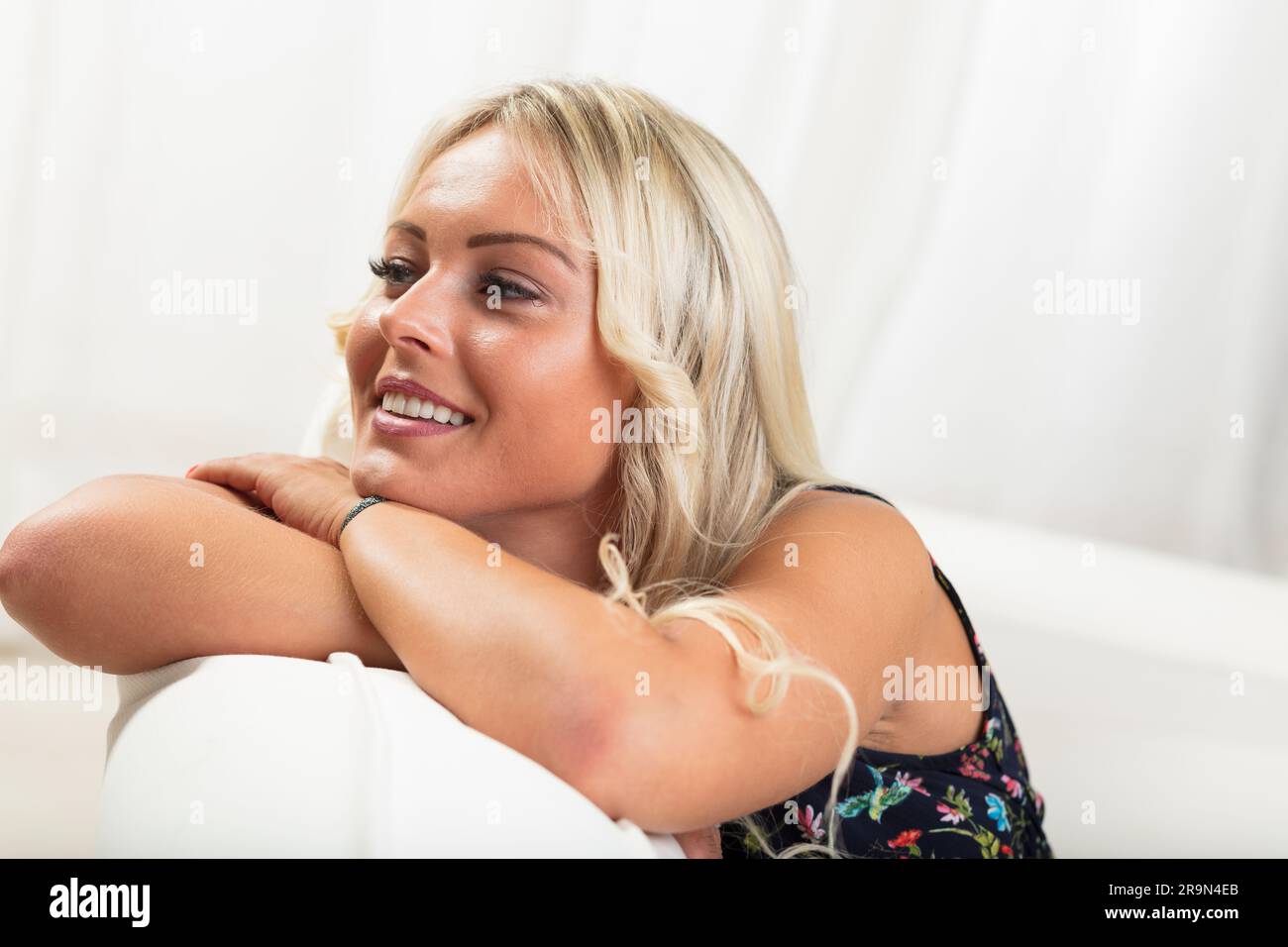 Languidly leaning blonde in a white living room. Perfect teeth visible ...