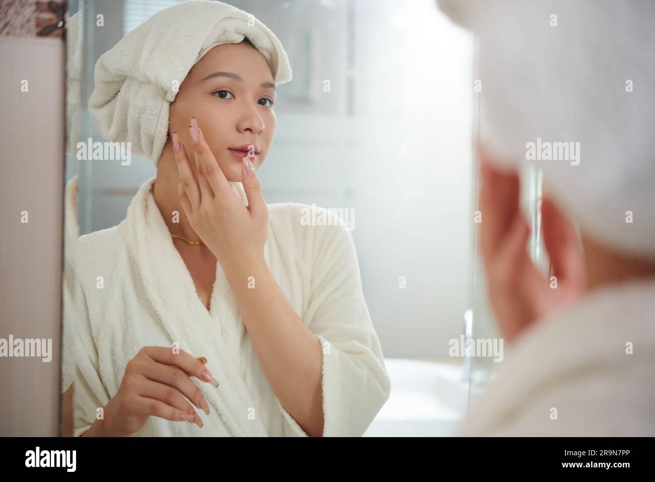 Transgender woman applying moisturizing lotion on face after morning ...