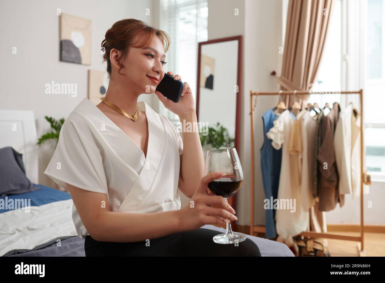 Smiling transgender woman dressed for event sitting on bed and talking ...