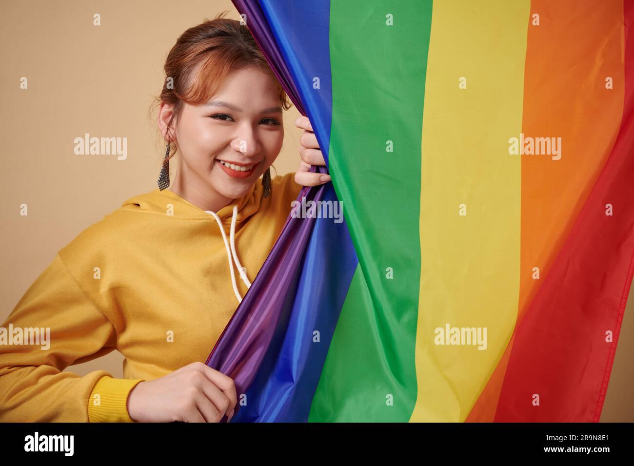 Portrait of happy transgender woman standing next to striped lgbt flag ...