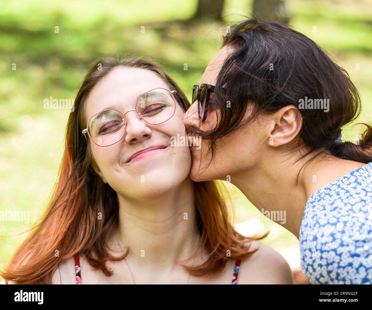 Mother Kissing Her Teenage Daughter With Dyed Hair And Glasses Against