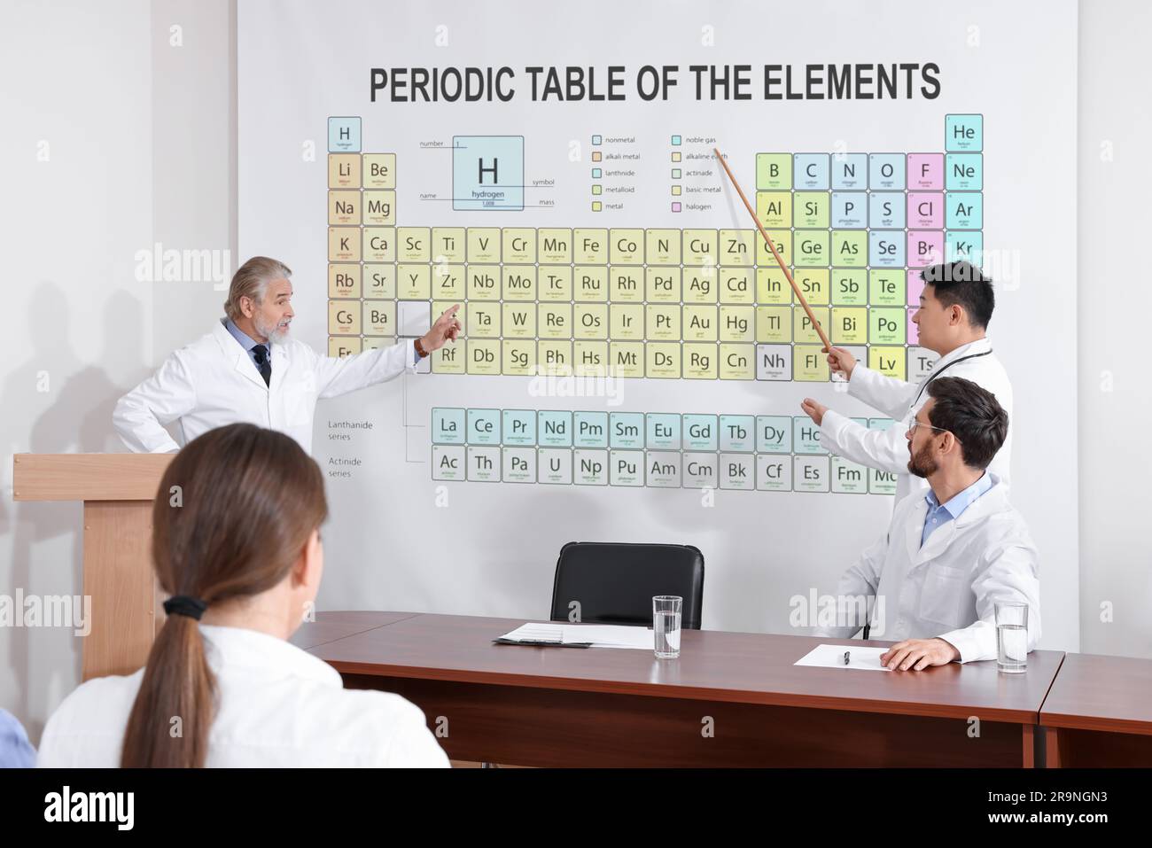 Lecture in chemistry. Professors using projection screen with illustration of periodic table to ...