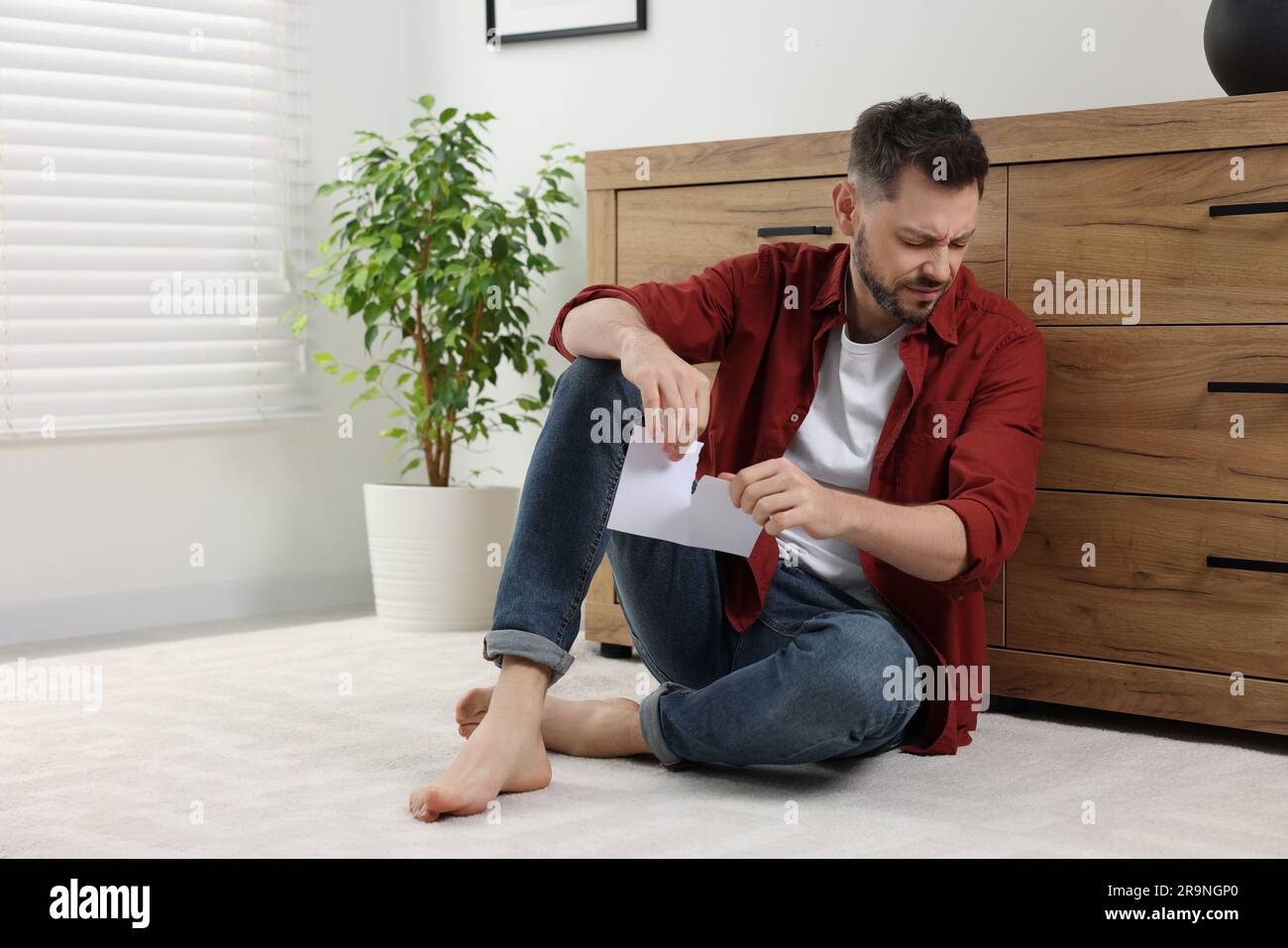 Sad man ripping photo on floor indoors, space for text. Divorce concept ...