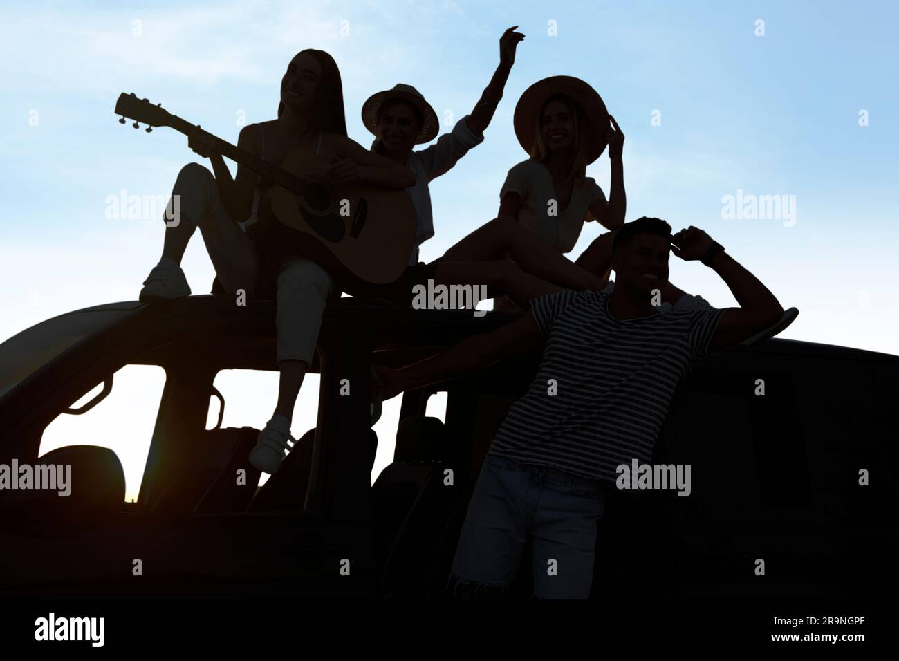Friends with guitar and car chilling outdoors. Silhouettes of people ...