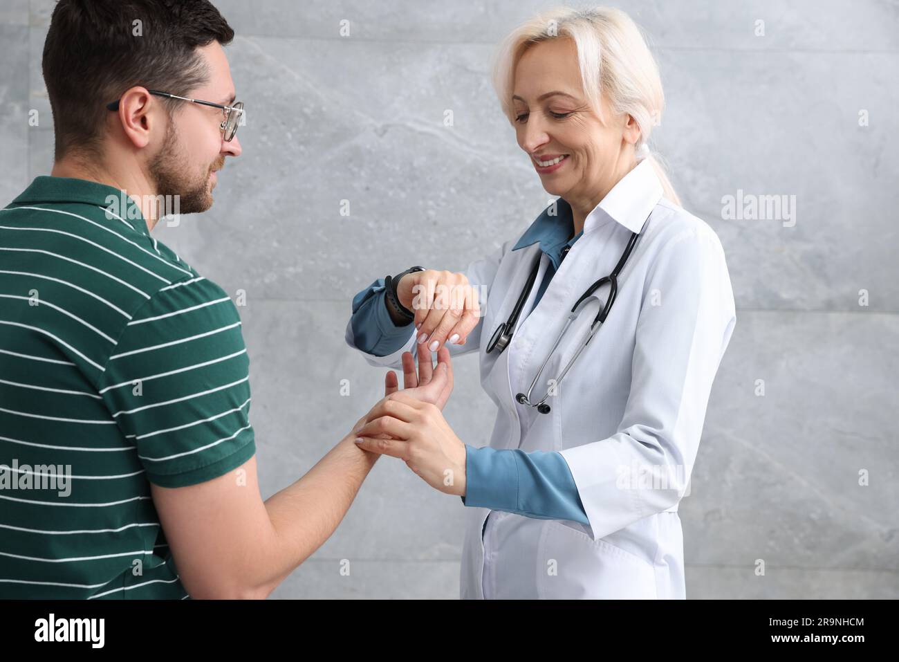 Doctor checking patient's pulse during consultation near grey wall ...