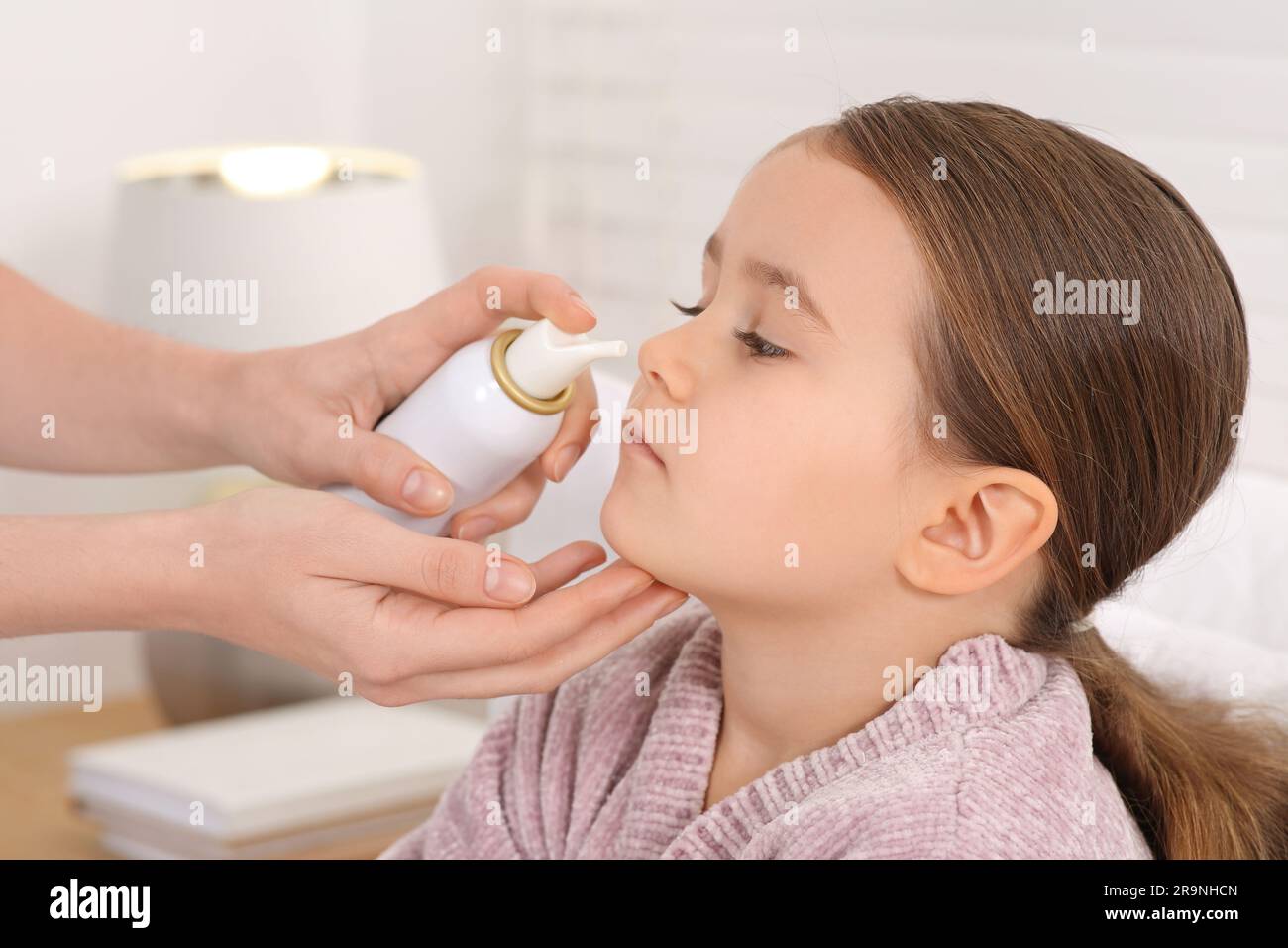 Mother using nasal spray to treat her little daughter indoors, closeup ...
